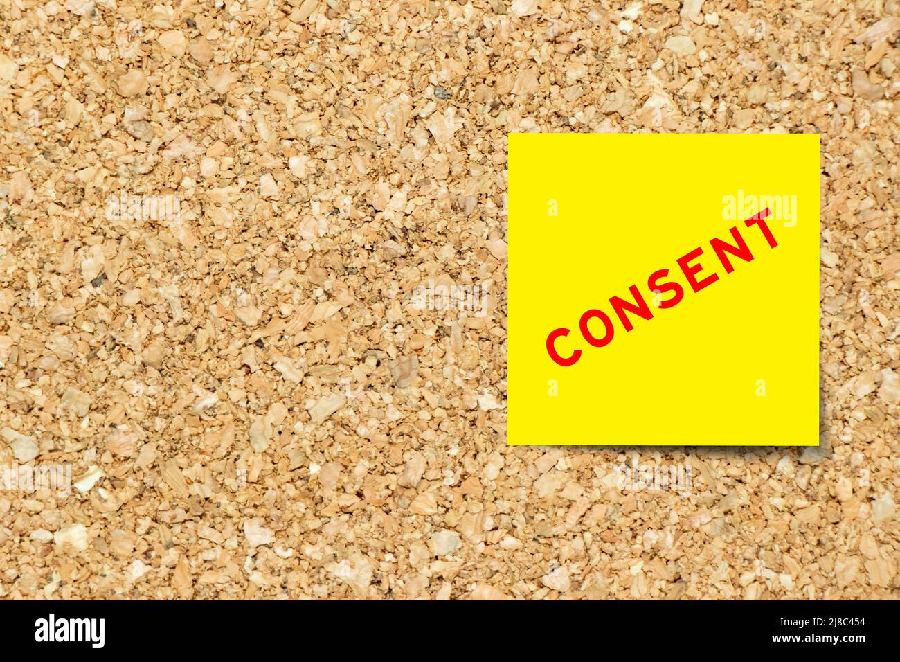 Yellow note paper with word consent on cork board background with copy ...
