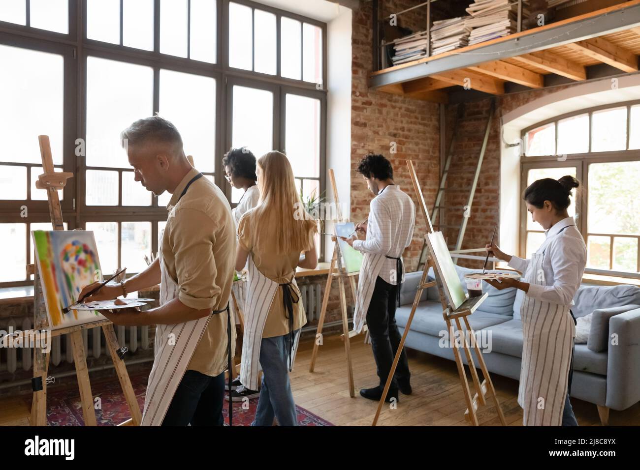 Back view five young multiethnic painters engaged in group art-class ...