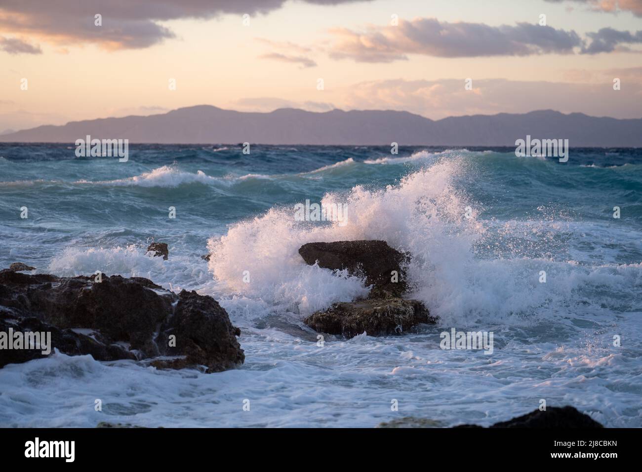 Sea wave at sunset hitting rock on the beach Stock Photo - Alamy