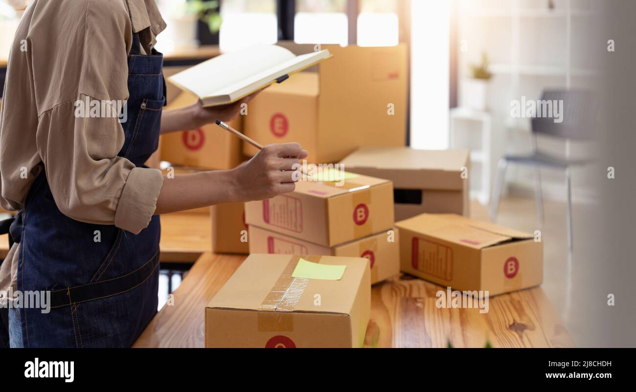 Young asian woman writing address on parcel box at home for delivery ...