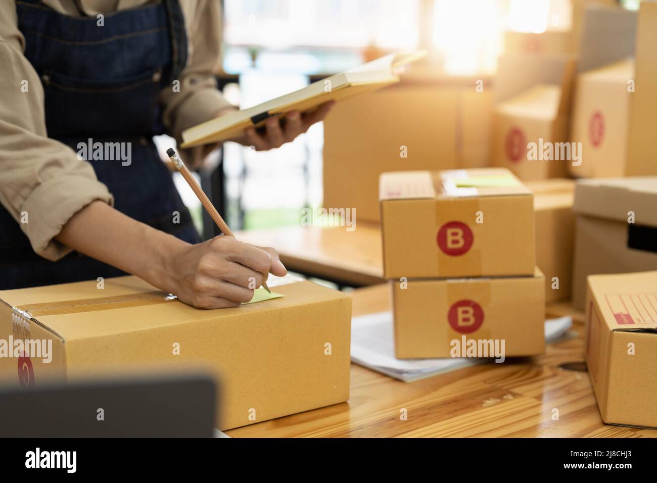 Young asian woman writing address on parcel box at home for delivery ...