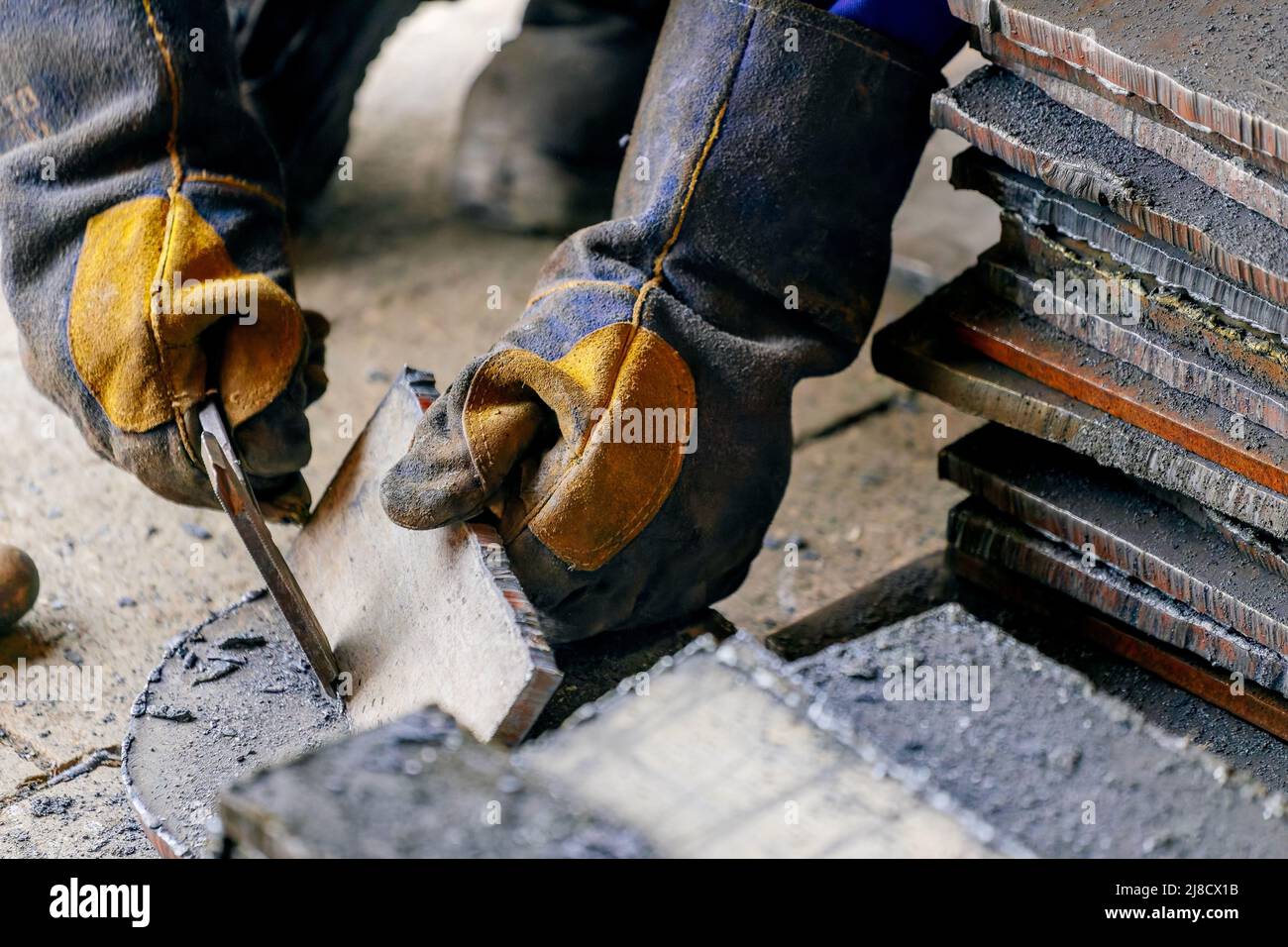 Worker in heavy industry or metallurgy beats scale off iron plates with ...