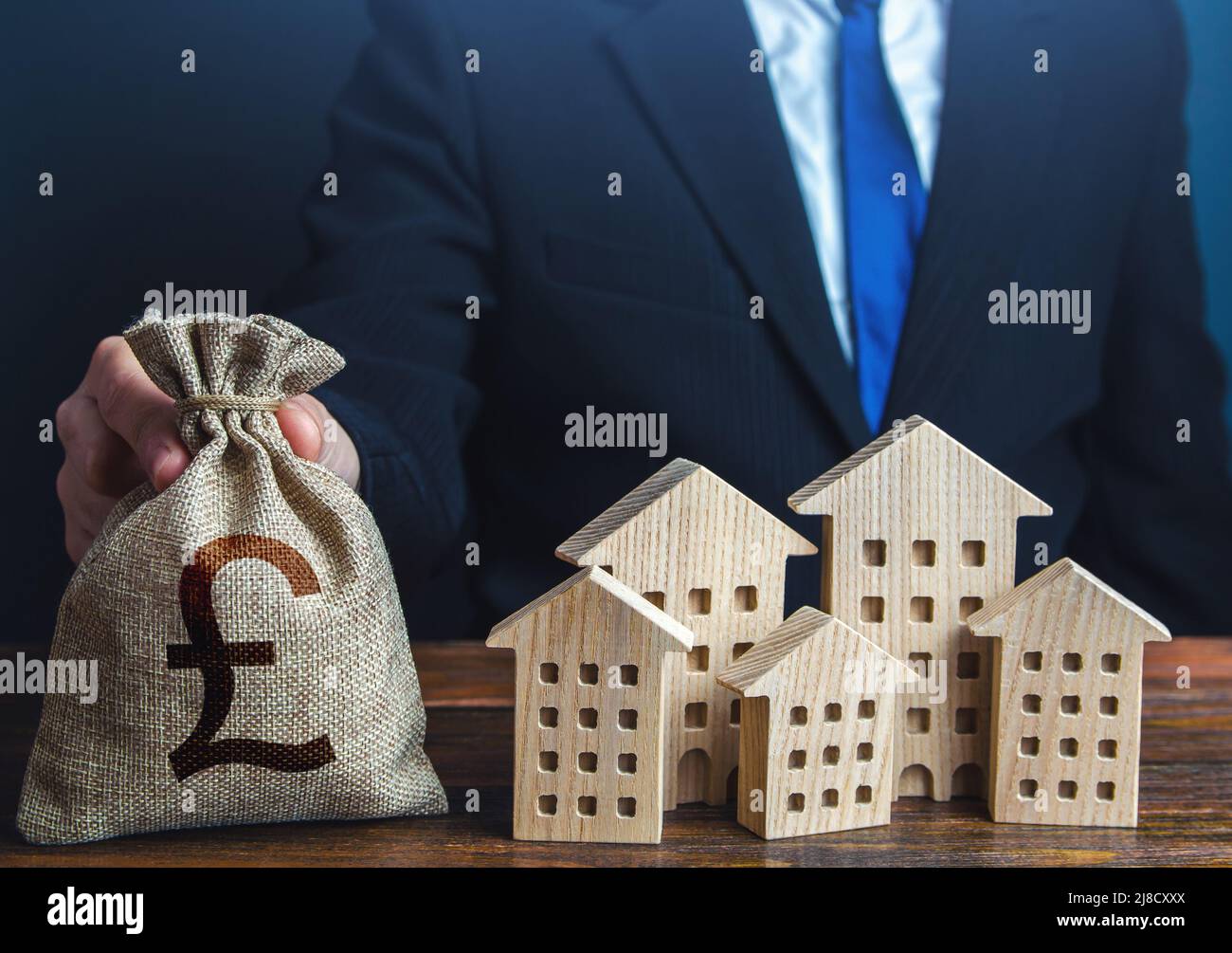 A businessman puts a british pound sterling money bag near the houses ...