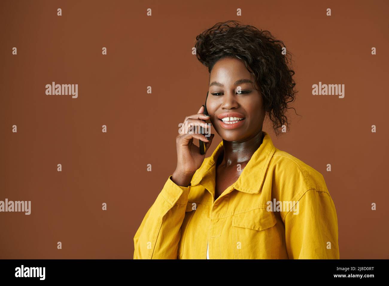 Smiling young woman in bright yellow jacket talking on phone with ...