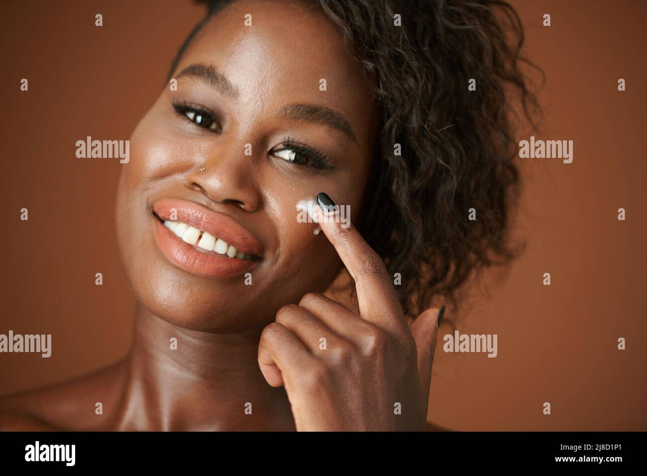 Face of happy young Black woman applying moisturizing lotion on face ...