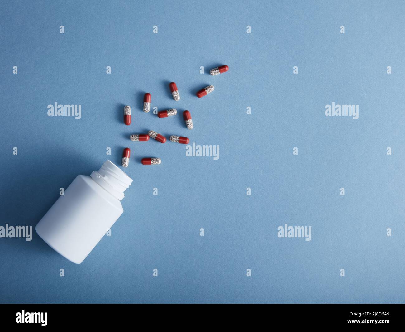 Capsules falling from the white bottle on blue paper background ...