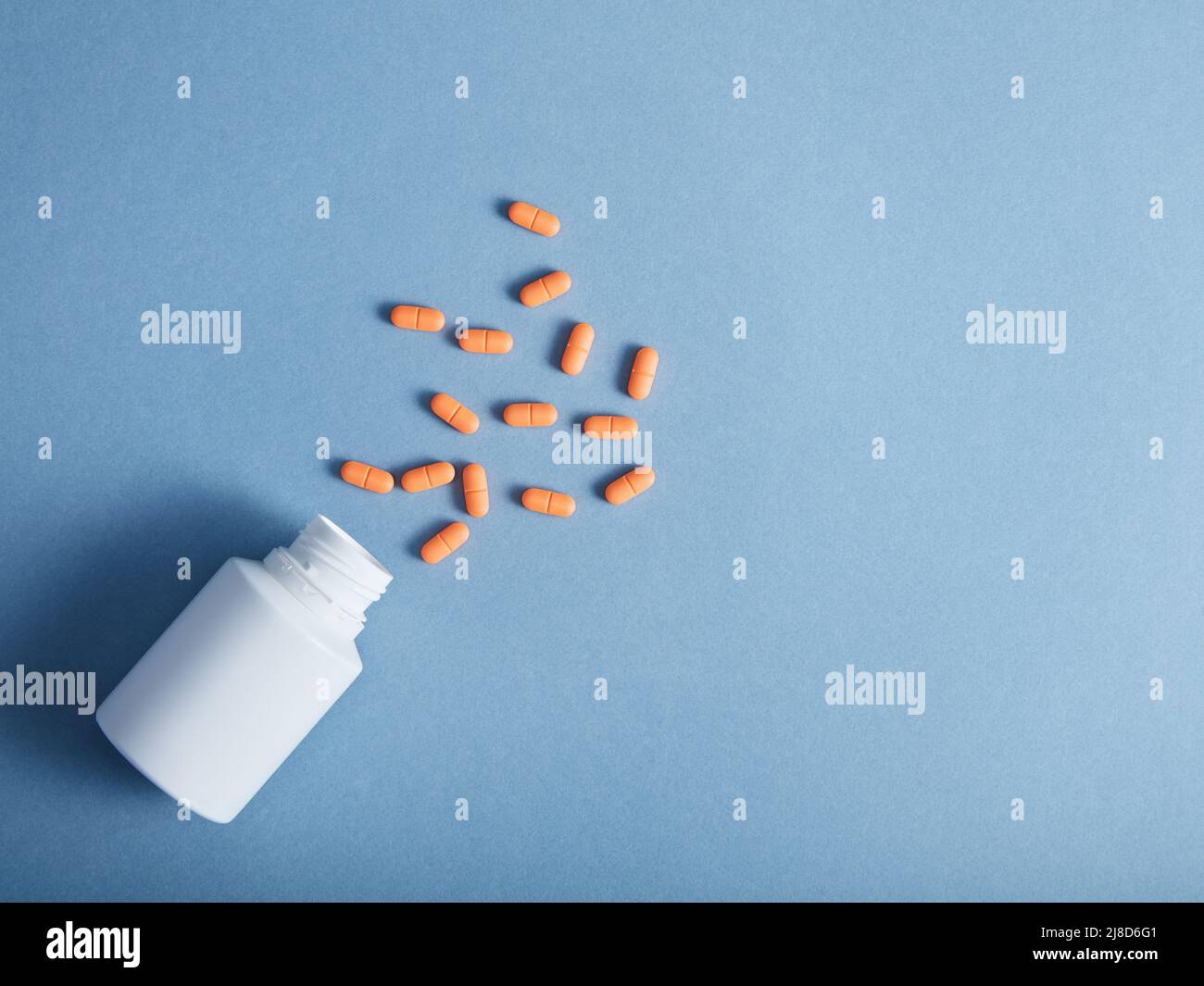 Capsules falling from the white bottle on blue paper background ...