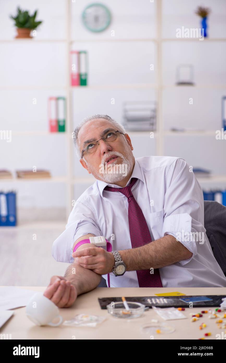 Old male drug addicted employee sitting at workplace Stock Photo - Alamy
