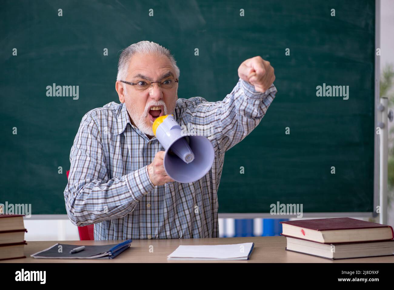 Aged male teacher holding megaphone in the classroom Stock Photo - Alamy