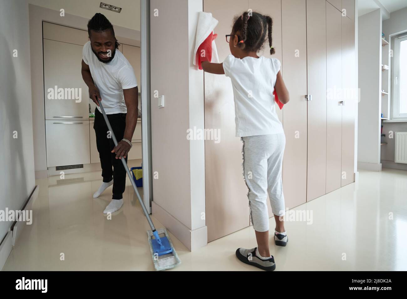 Adult African American man is mopping floor near his lottle daughter ...