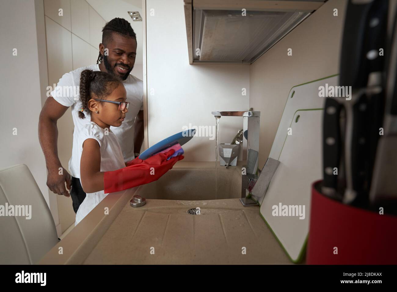 Adult man watching his daughter wash plate in the sink Stock Photo - Alamy