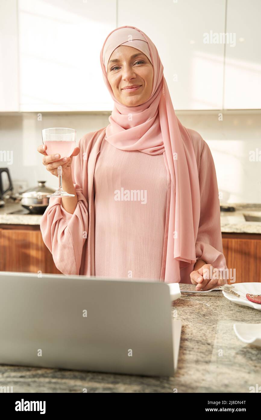 Muslim woman with drink using notebook in kitchen Stock Photo - Alamy