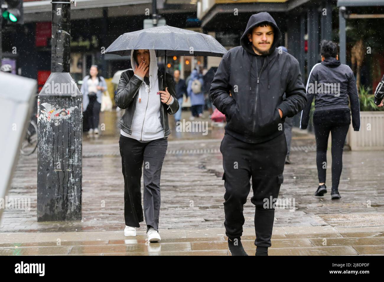 A woman smoking protects herself from the rain under an umbrella on a ...