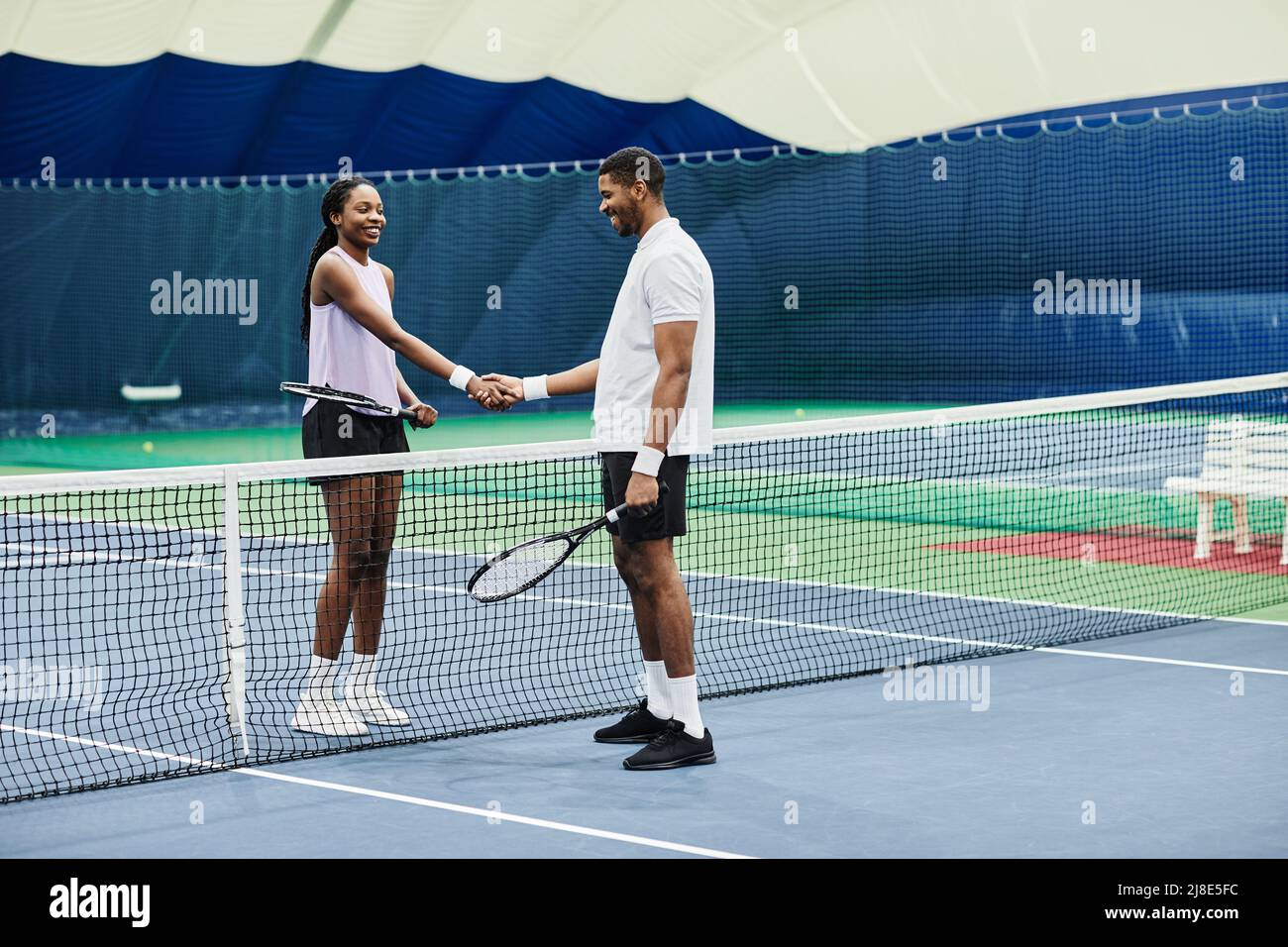 Full length shot of two tennis players shaking hands across net during ...