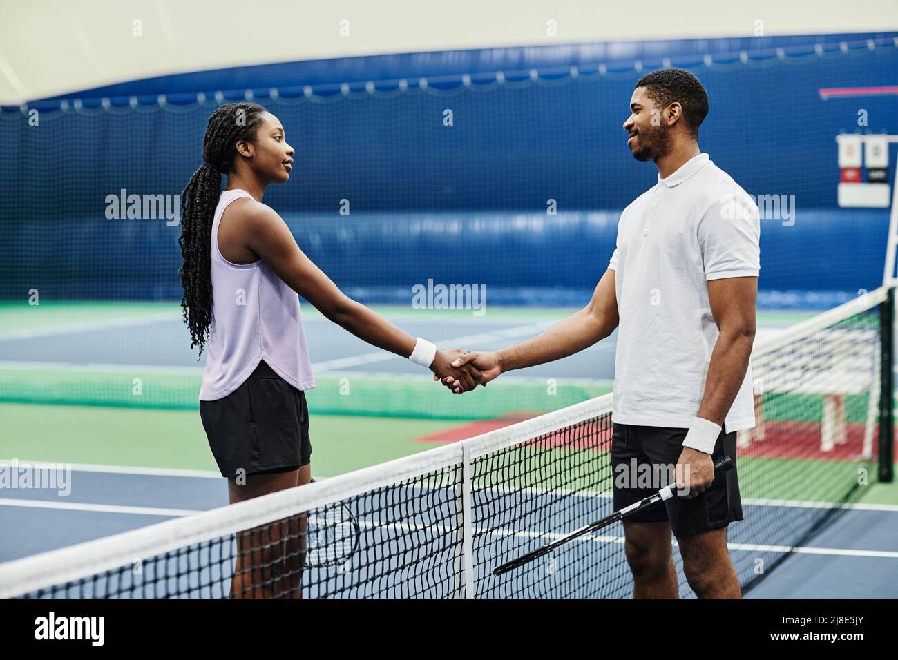 Side view portrait of two tennis players shaking hands across net ...