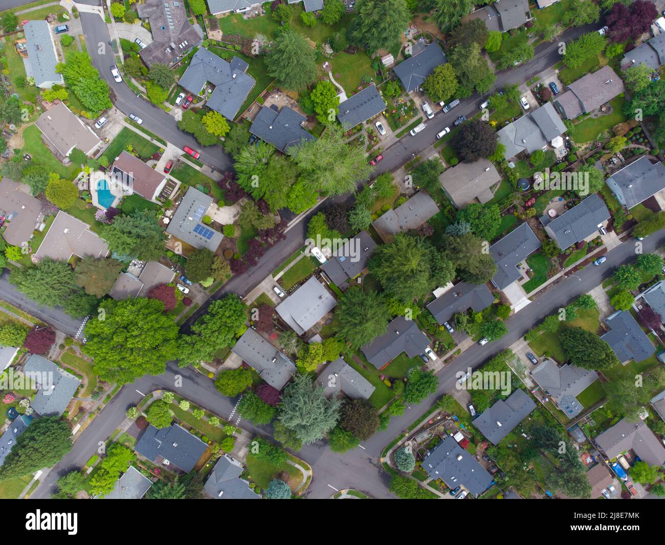 Drone shot. Small town, suburb. Lots of greenery, paved roads, roofs of ...