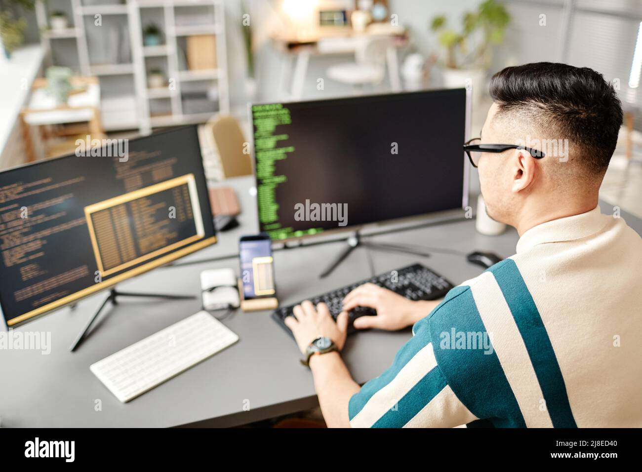 High angle view at Asian IT developer typing on keyboard with programming code on computer ...