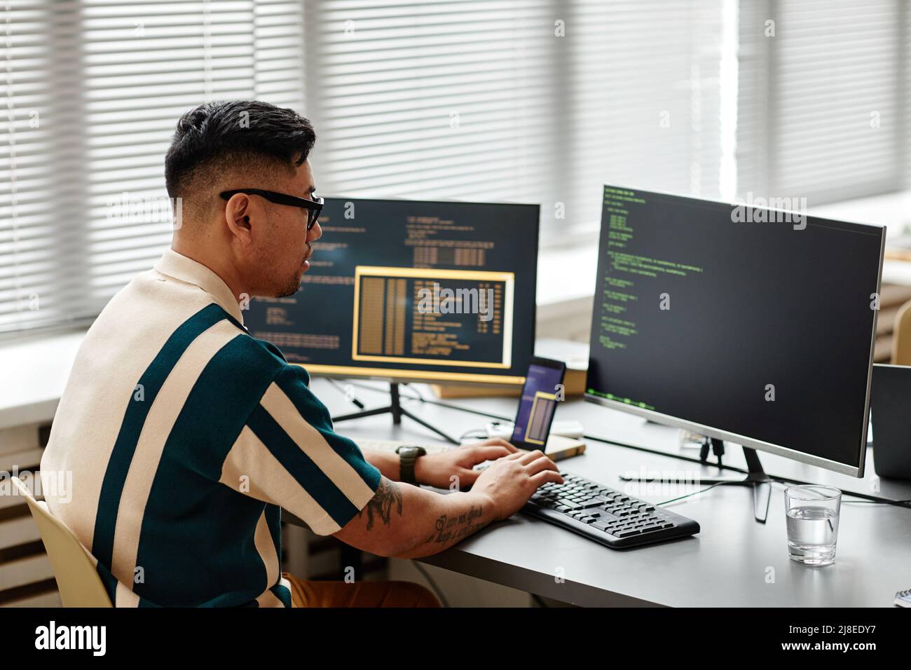 Side View Of Asian It Developer Typing On Keyboard With Programming Code On Computer Screen