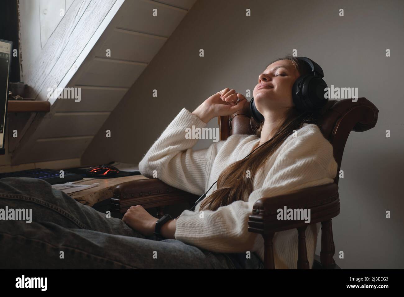 Young woman listening to music in big headphones near computer at home ...