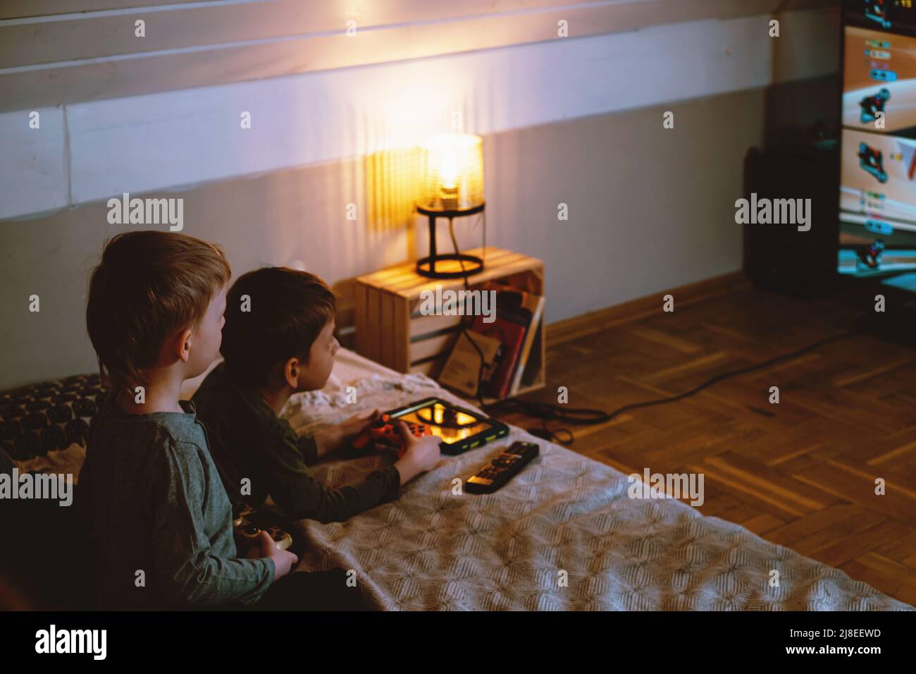 Kids playing video games at home on the bed at night. Boys using game ...