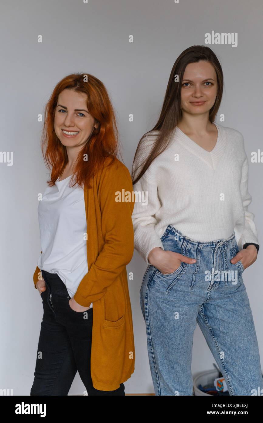 Happy two women in their 20s 40s over white wall. Employees in casual ...