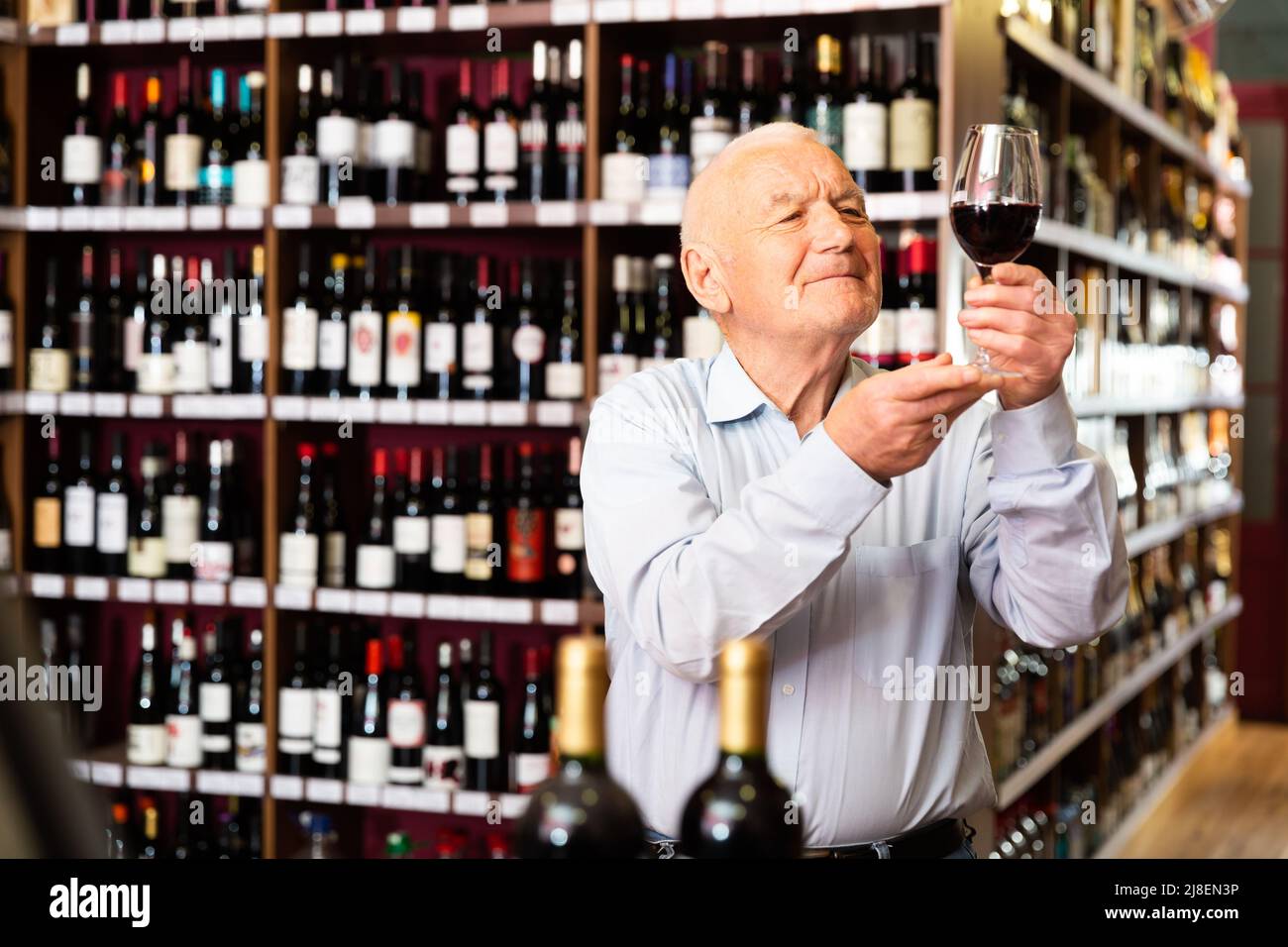 Elderly man checks the color and taste of red wine in a liquor store ...
