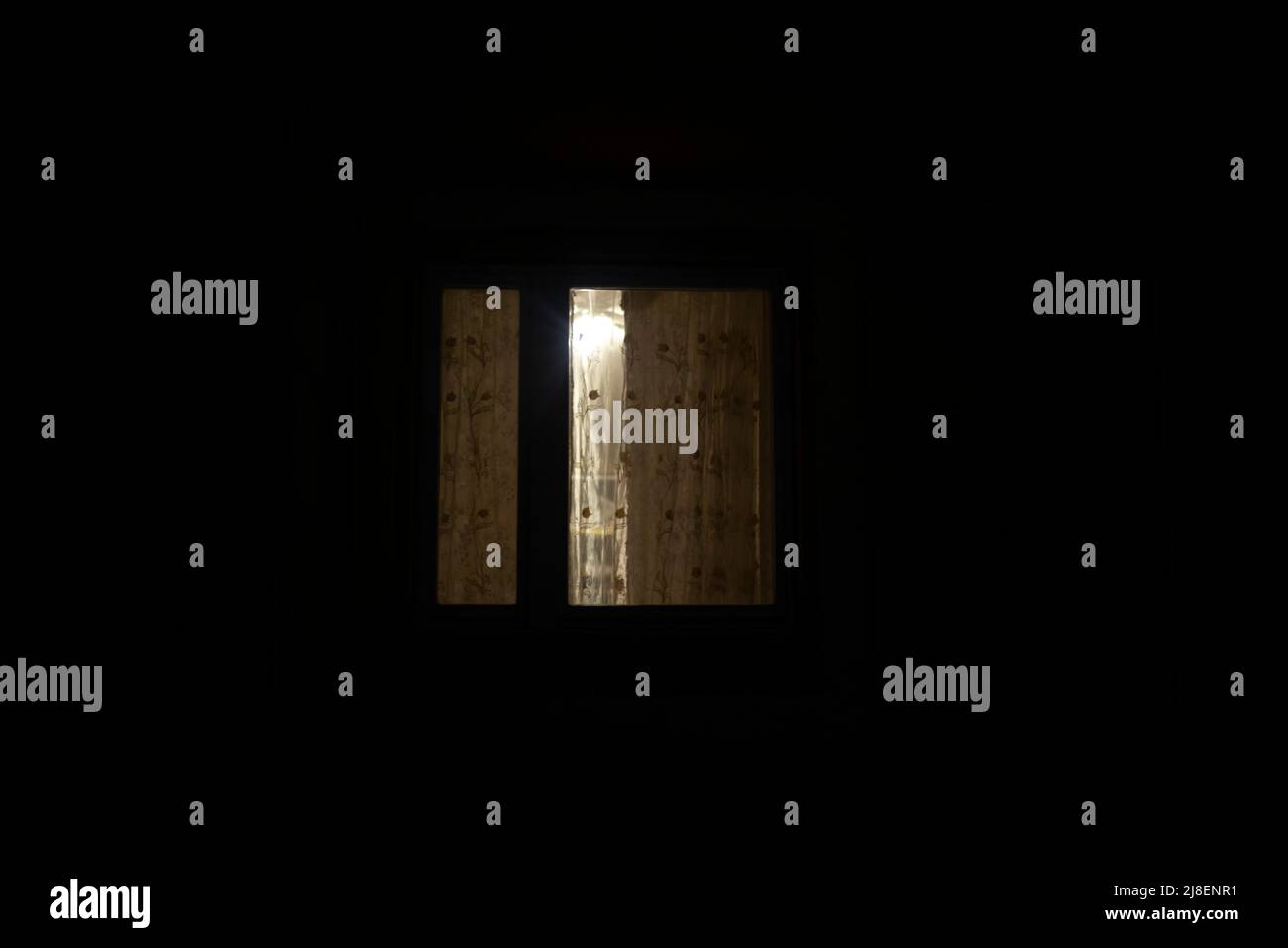 Window is in dark. Curtains on window at night. Light behind glass ...
