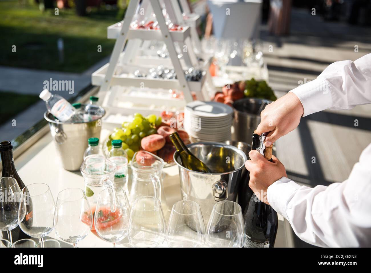 The waiter opens a bottle of alcohol on the table Stock Photo - Alamy