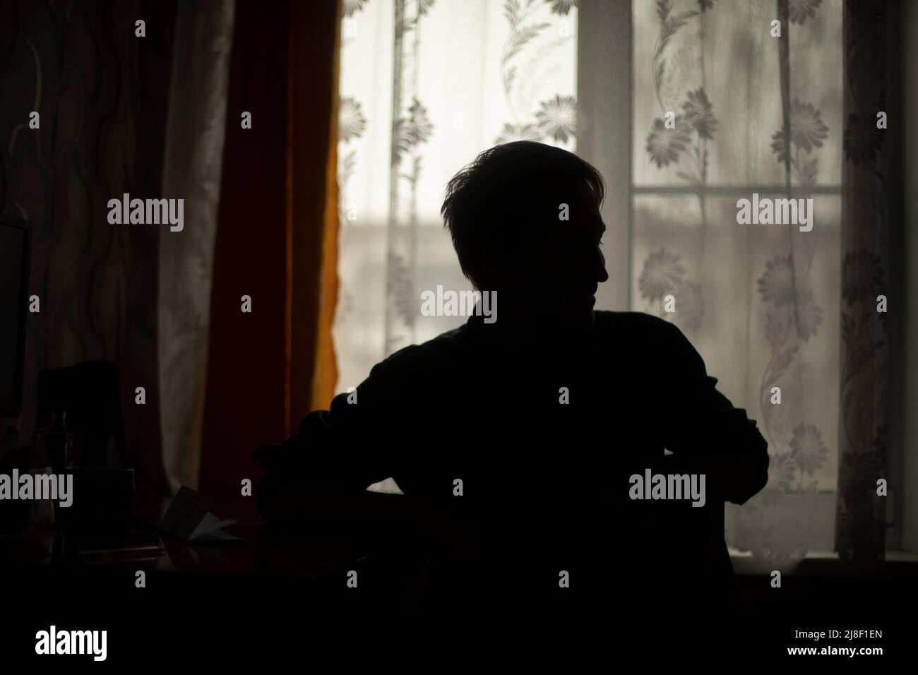 Silhouette of guy in room. Guy sits by window. Shadow of man. Dark room ...