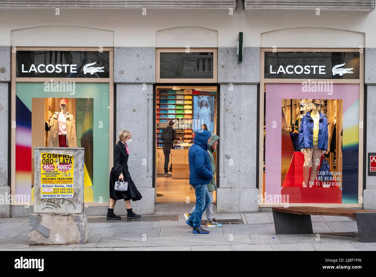 Pedestrians walk past the French clothing brand Lacoste store and logo ...