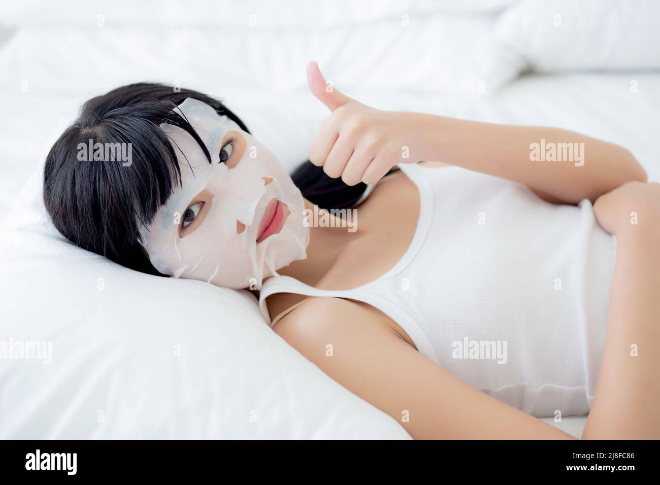 Beautiful young asian woman with sheet facial mask and thumbs up on bed ... Beautiful young asian woman with sheet facial mask and thumbs up on bed ...