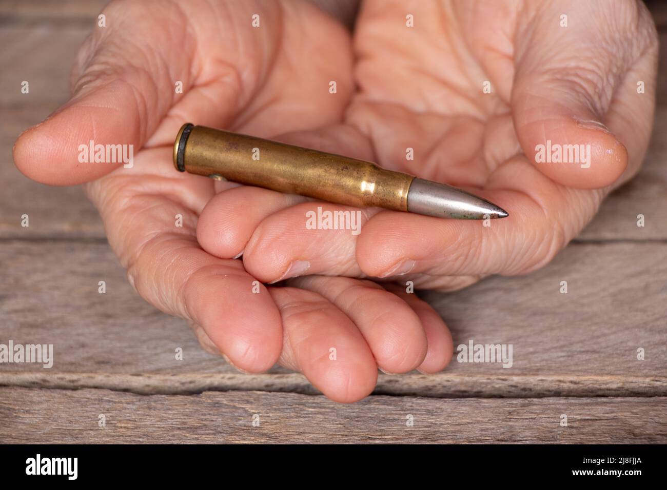 The hands of an old woman hold a military bullet on a wooden background ...