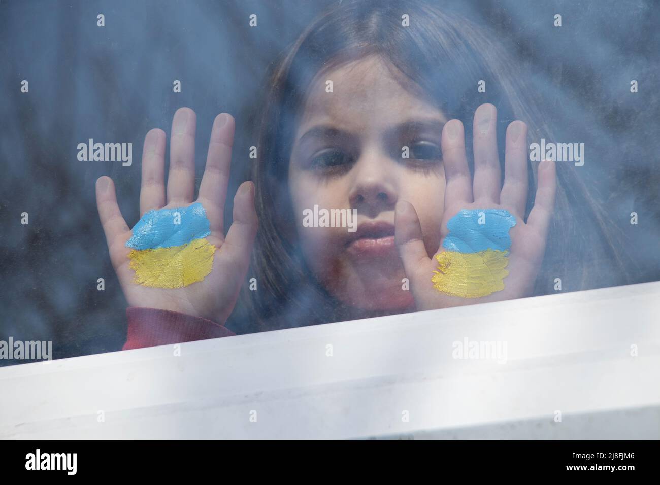 A little girl in the window of her house with a painted yellow-blue ...