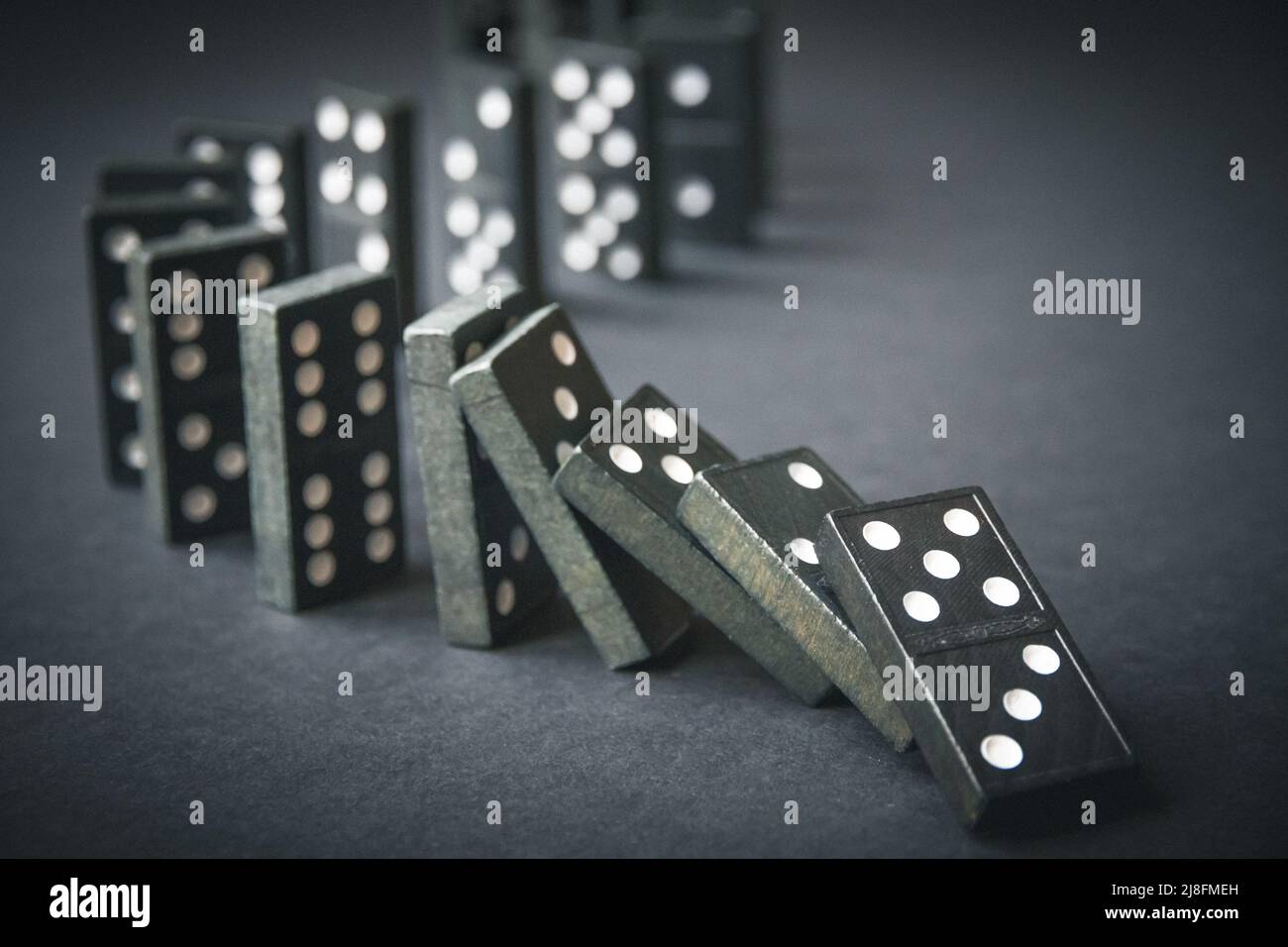 Black dominoes chain on a dark table background. Domino effect concept ...