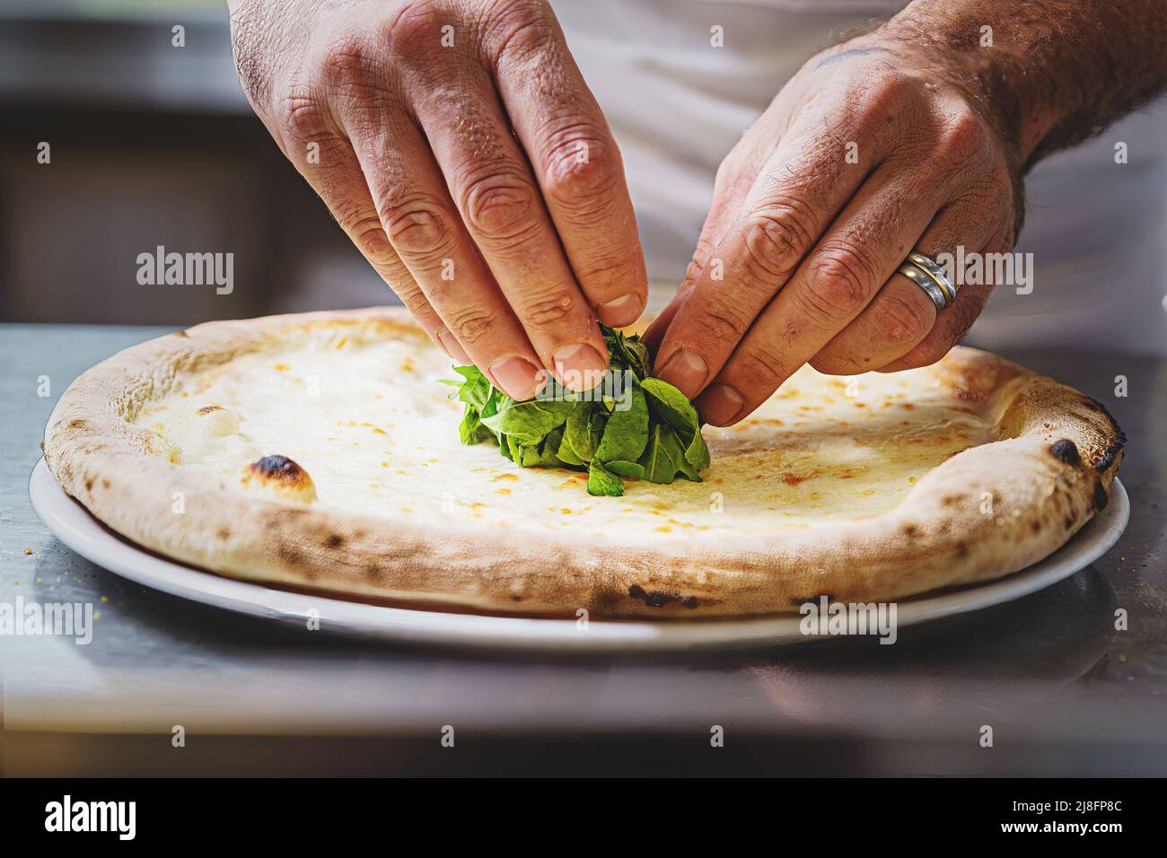 Chef garnishing an Italian pizza with rucola vegetables - closeup on ...