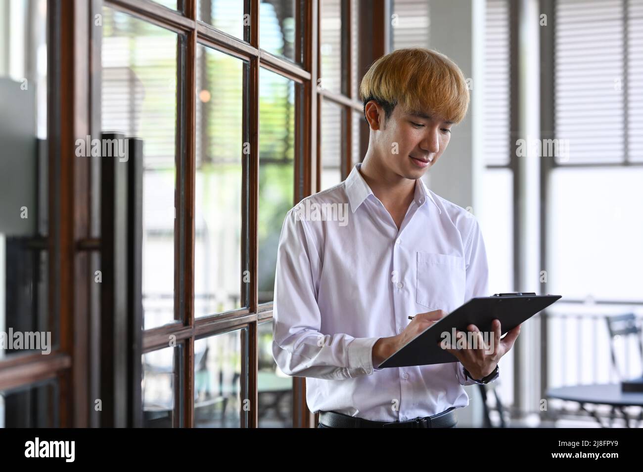 Asian male office worker reading information on clipboard while ...