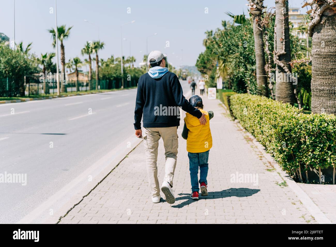 Rearview of father and son walking near city road. Dad holding his kid ...