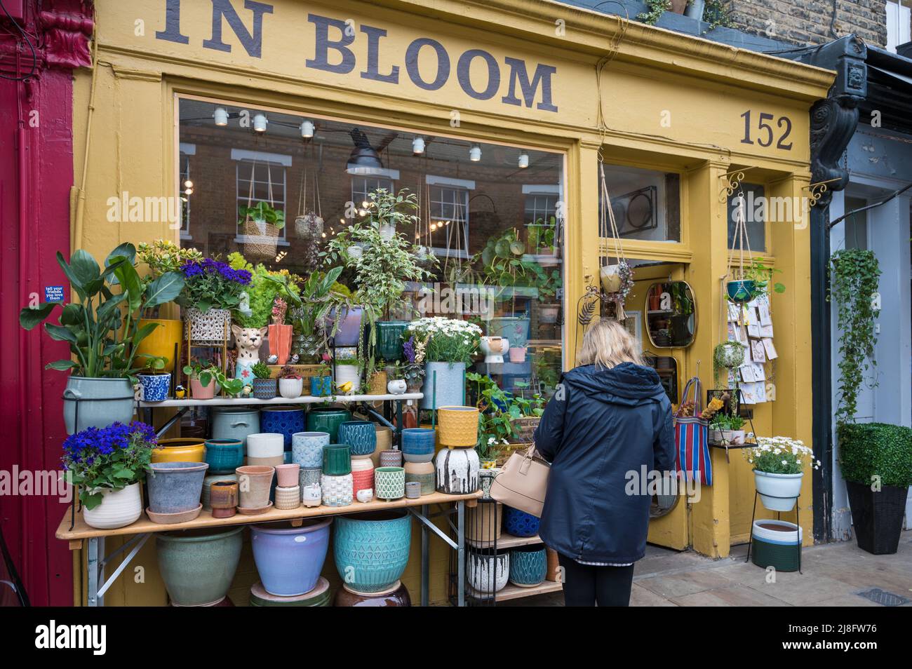 Lone woman browsing the pavement display of goods outside the In Bloom shop on a Sunday market ...