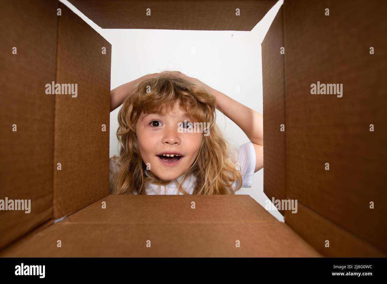 Funny excited child unpacking and opening the carton box looking inside ...