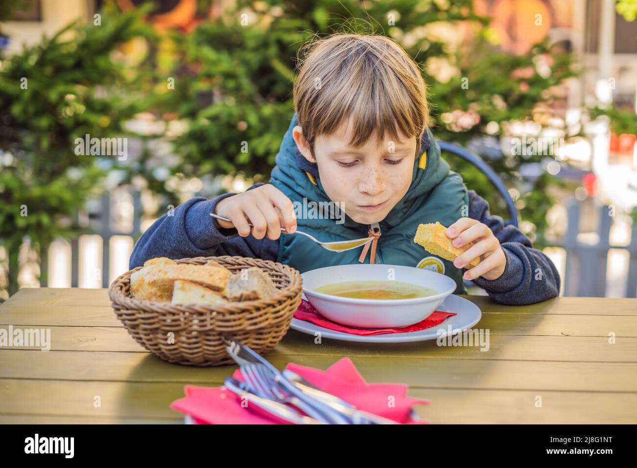 Adorable little school boy eating vegetable soup outdoor. Blond child ...