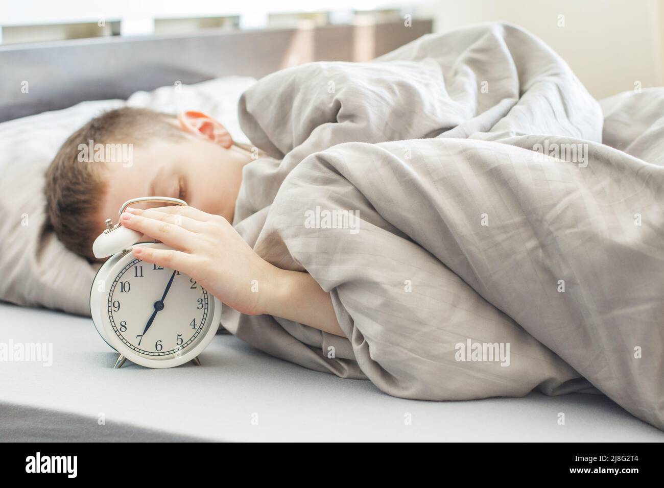 boy lying on the bed and stopping alarm clock in the morning. childs ...