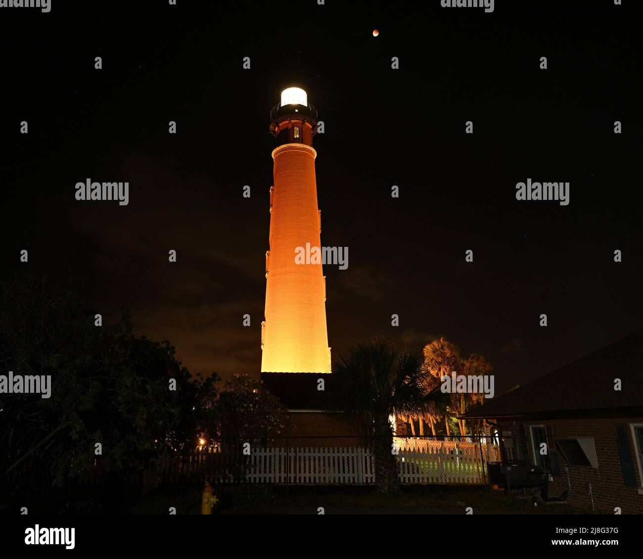 An eclipsed moon hangs over the historic Lighthouse in Ponce Inlet ...