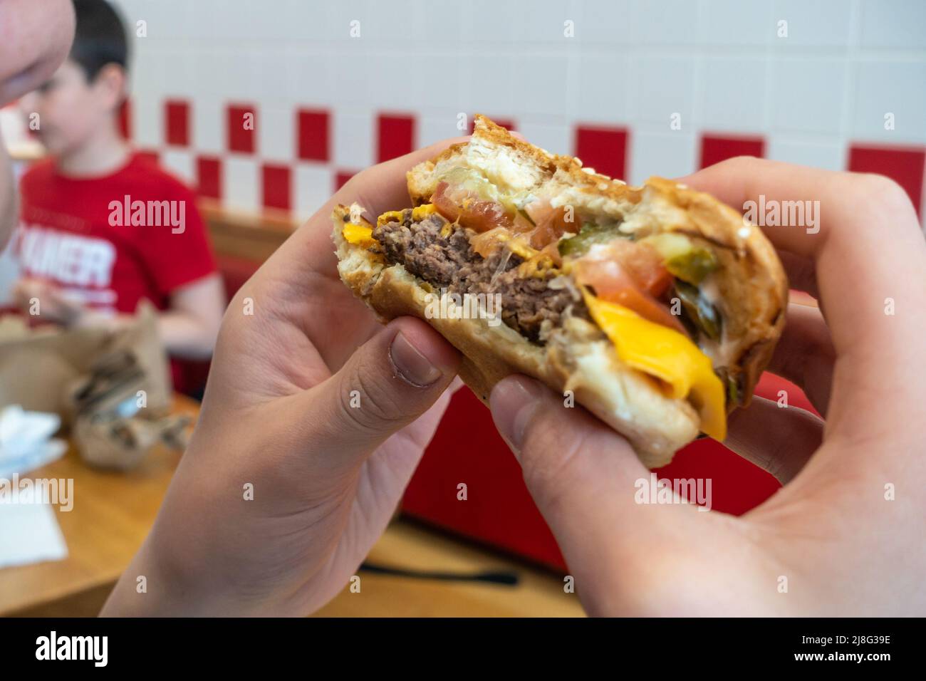 Looking over the shoulder of a child eating a cheeseburger at a fast ...