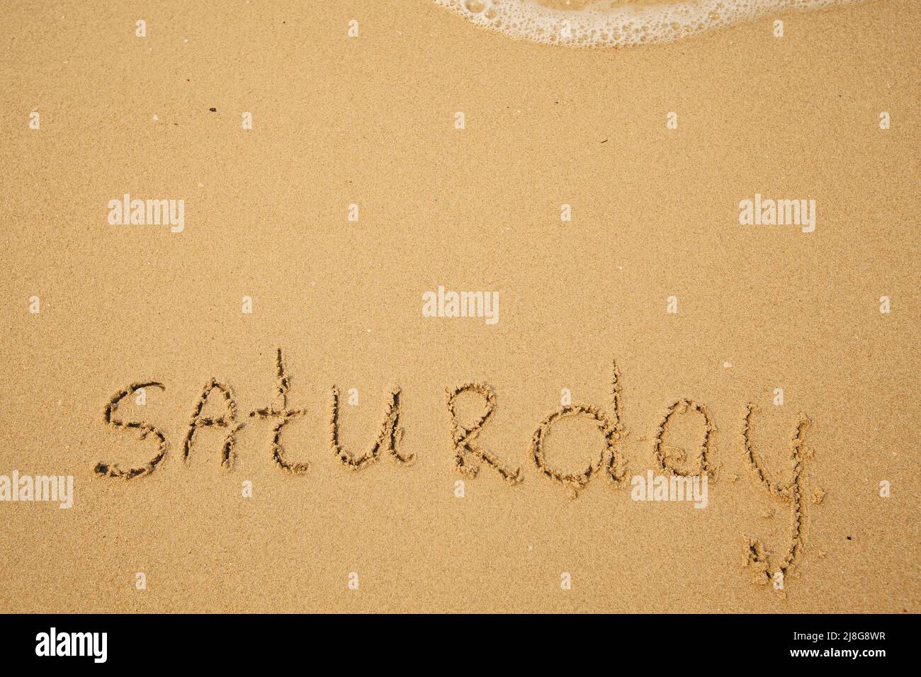 Saturday - drawing of days of the week, handwritten on the sea beach ...