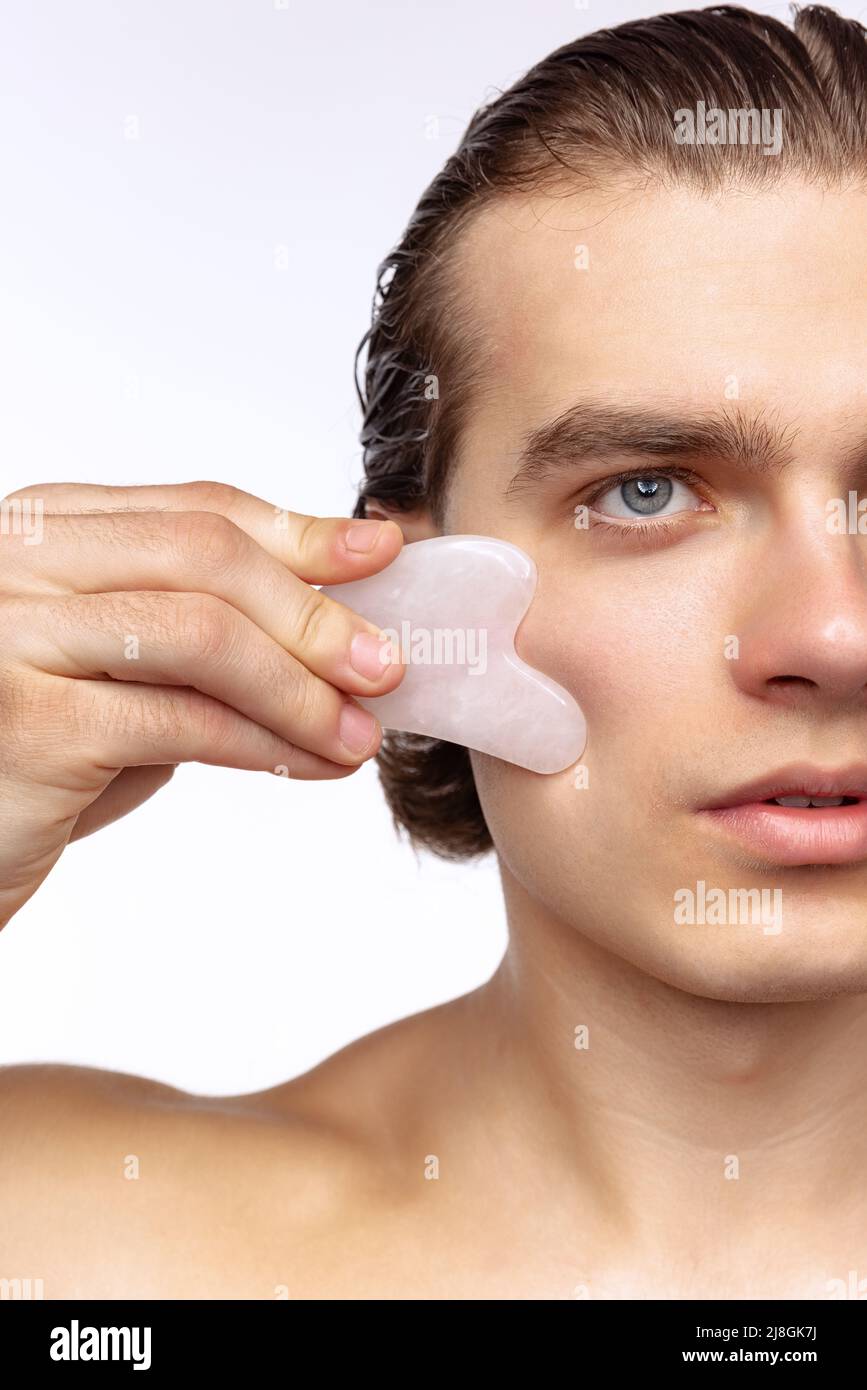 Young attractive man with perfect smooth skin, applying face massagers ...