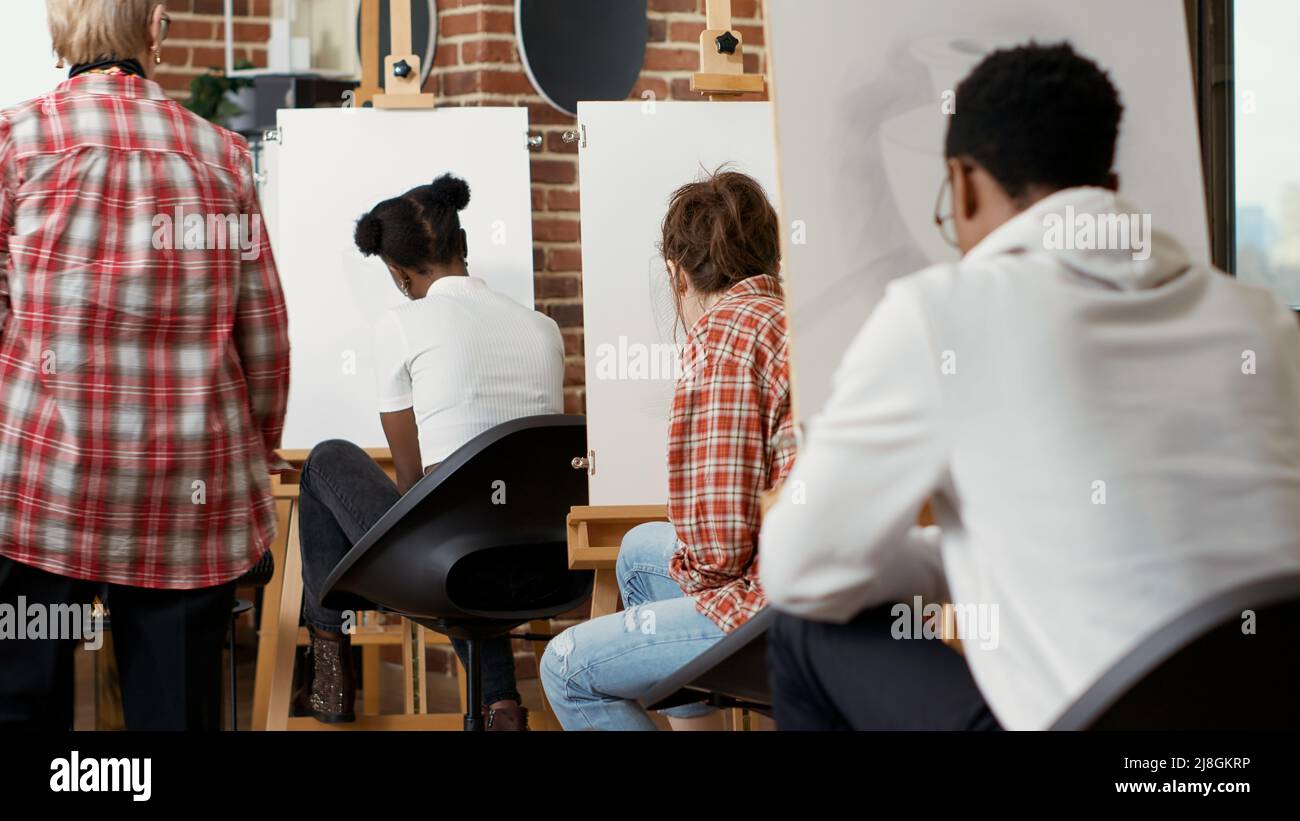 Elder artist helping young student with vase model drawing in creative ...