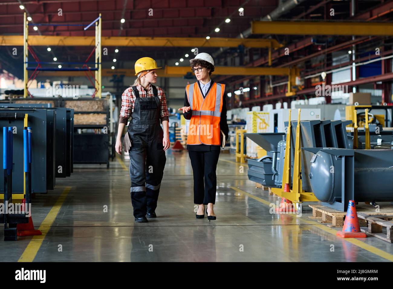 Two young workers of modern industrial factory having discussion of ...