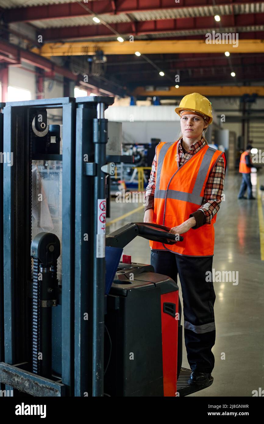 Young woman in hardhat, coveralls and orange jacket standing on ...