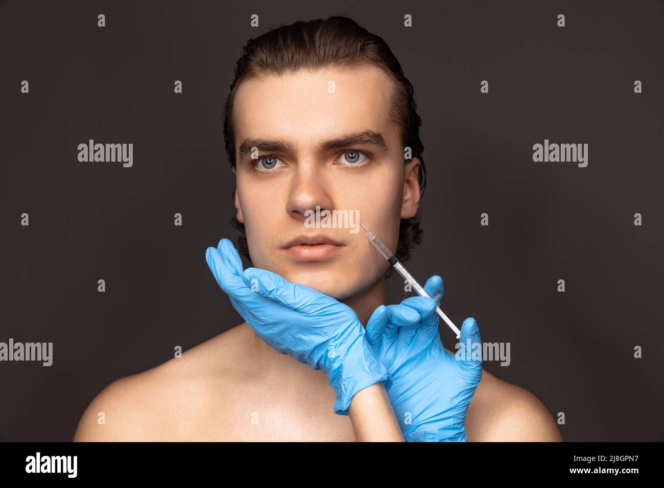 Close-up face of young man and female hands in blue gloves with syringe ...