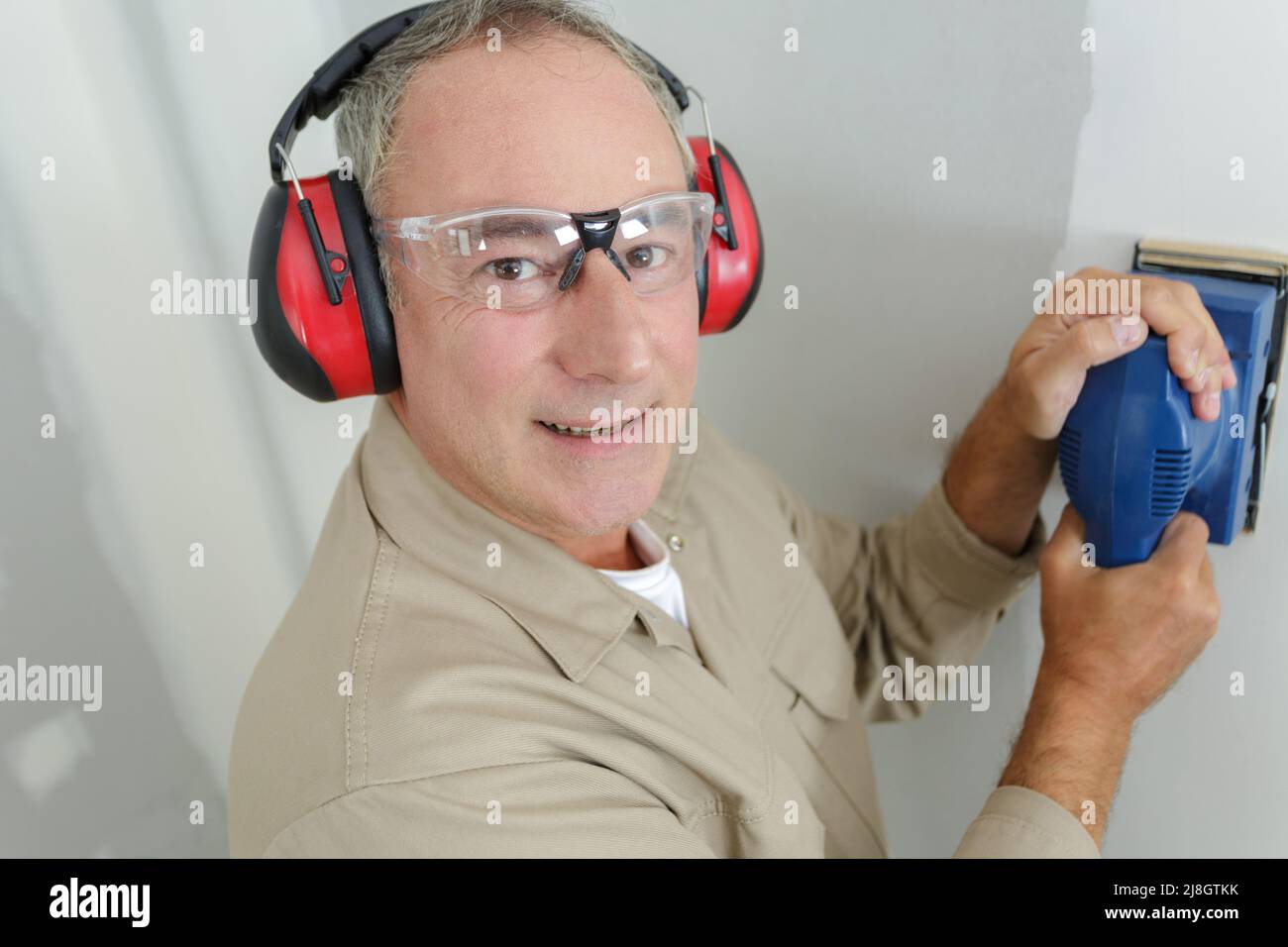 man sanding a wall with a power sander Stock Photo - Alamy